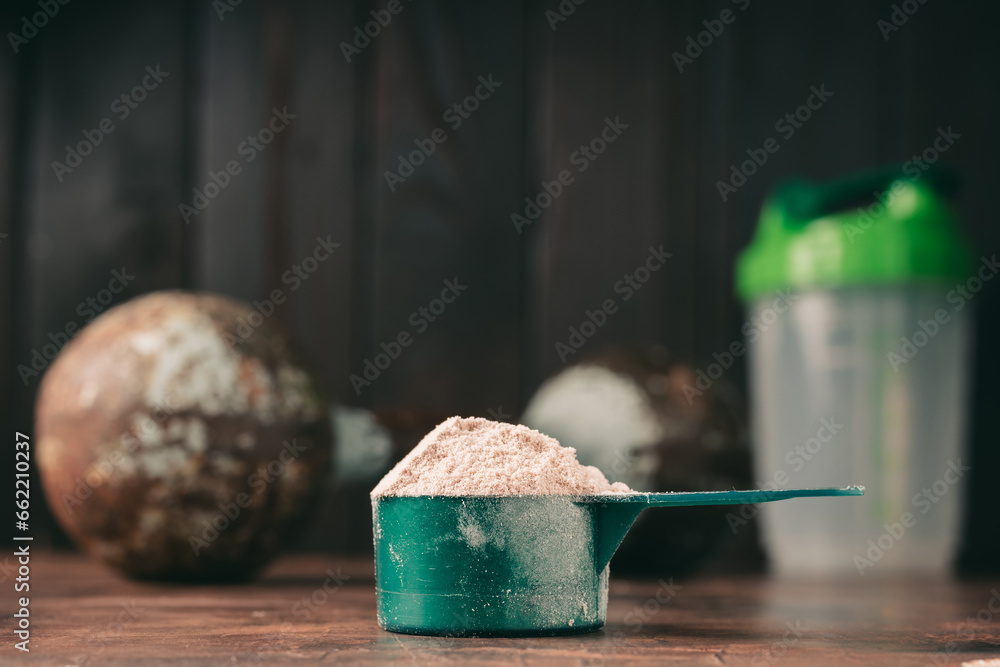 Chocolate whey protein powder in measuring spoon, old rusty dumbbell ...