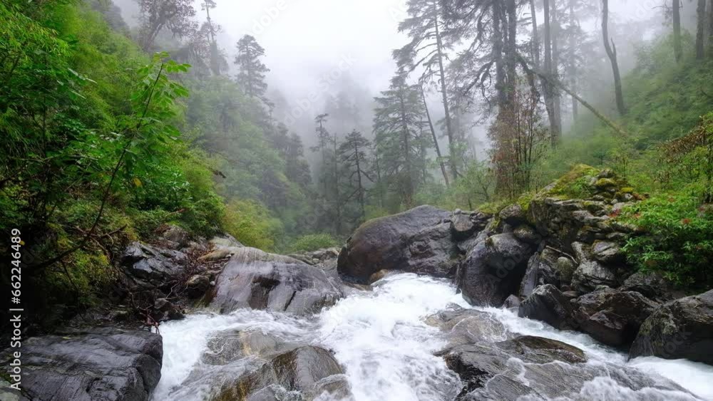 Powerful mountain creek running through the big boulders down the foggy ...