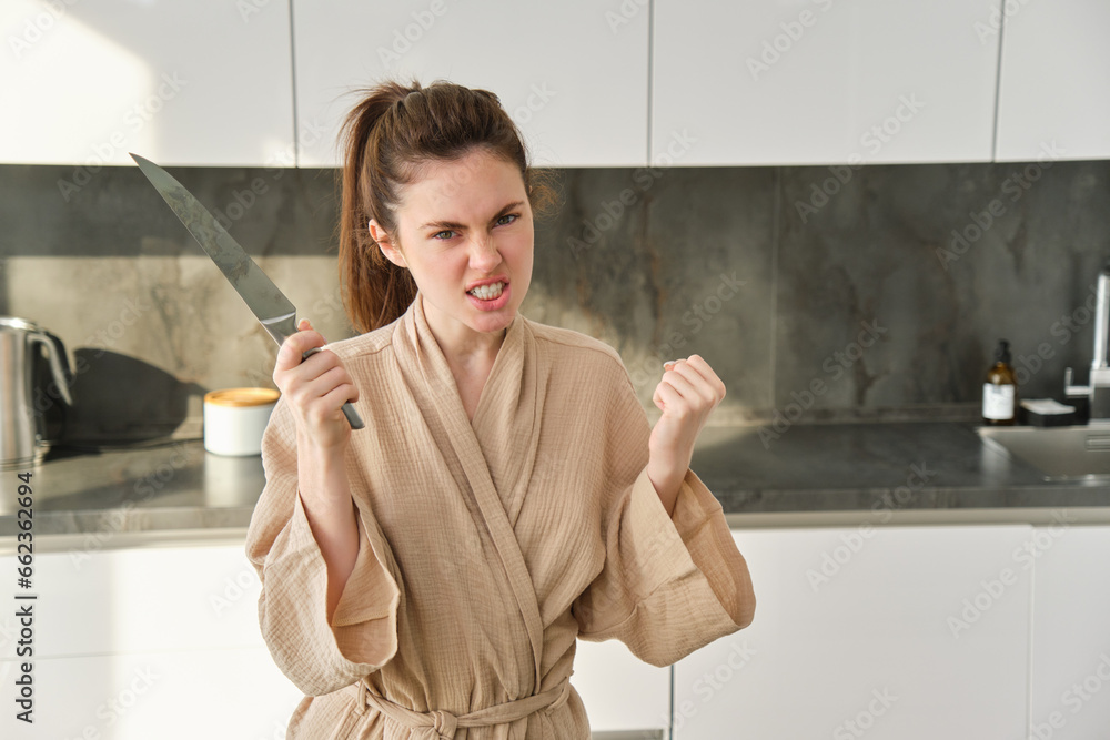 Portrait of annoyed woman with knife, angry while cooking in the ...