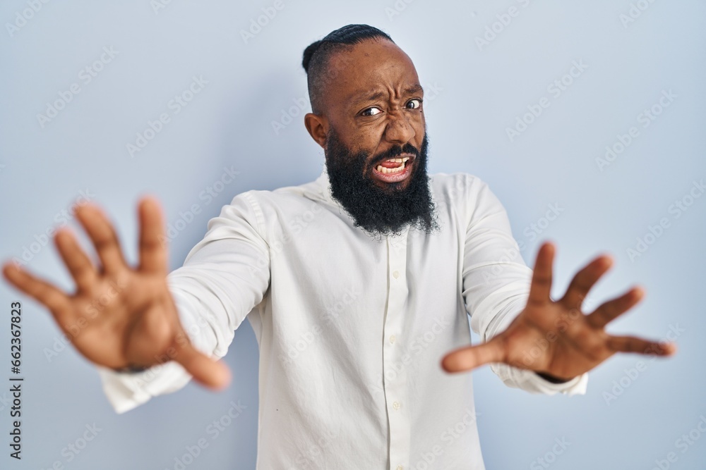 African american man standing over blue background afraid and terrified ...