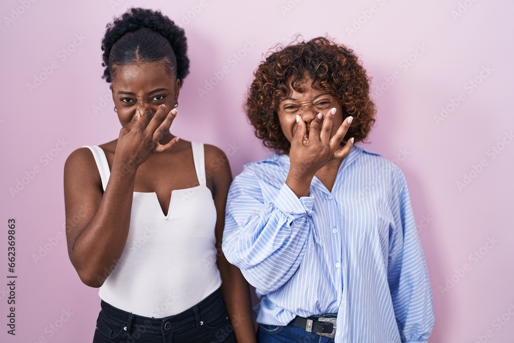Two african women standing over pink background smelling something ...