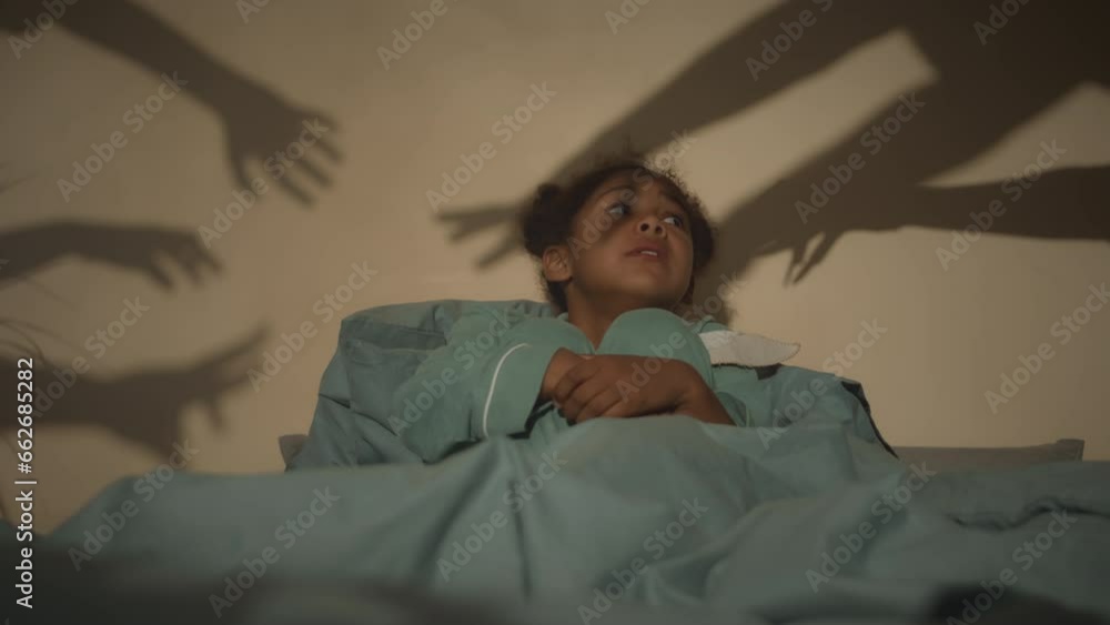 Slowmo of scared African American little girl sitting on bed in dark ...