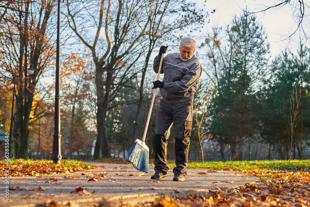 Maintenance worker cleaning roads and alleys with plastic garden broom ...