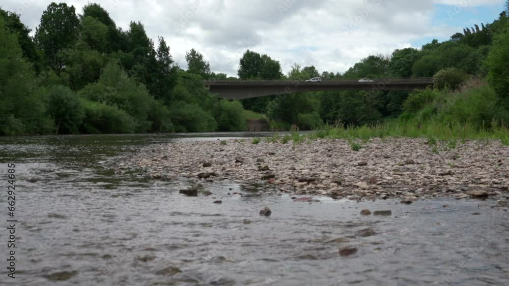 A British river scene with passing cars on a bridge in the background ...