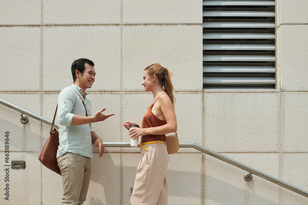 Smiling young Asian man asking out young woman when that are standing ...