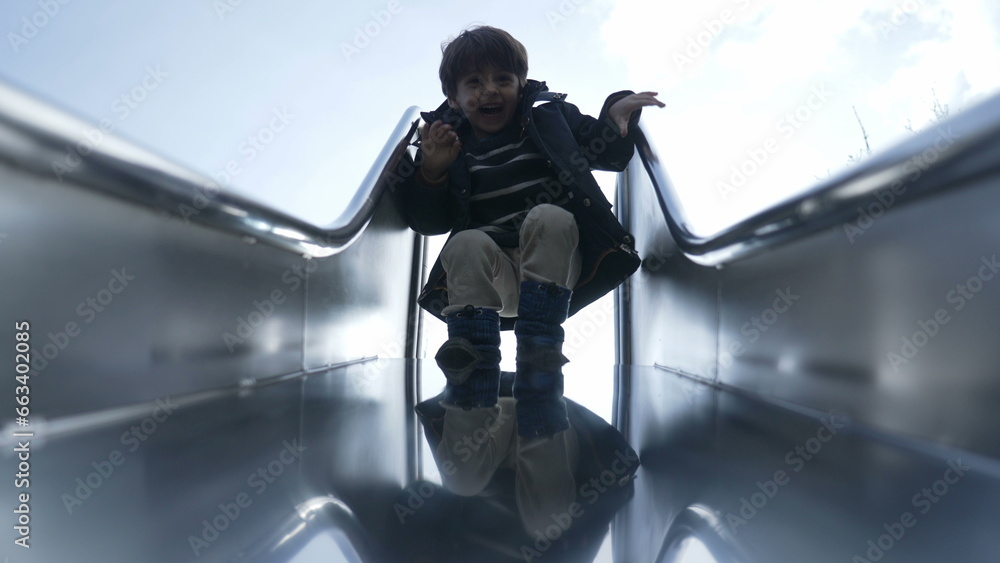 Joyful child sliding down slider at playground park during fall season ...