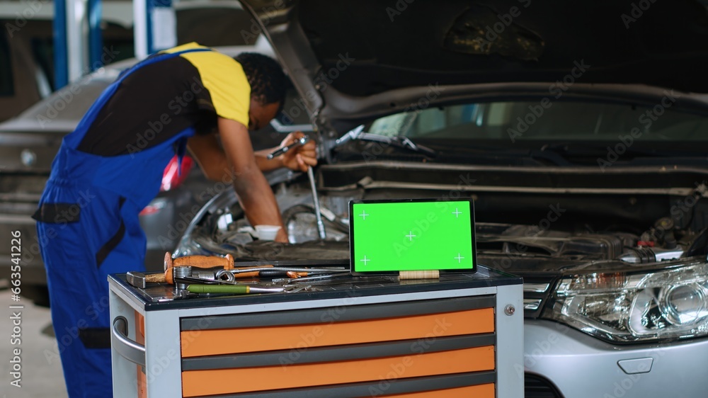 Engineer in car service uses torque wrench to secure bolts inside vehicle with green screen ...