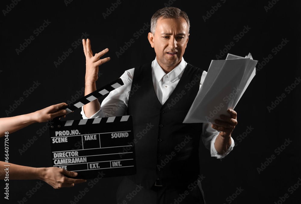 Mature actor reading script and hands with clapperboard on dark ...