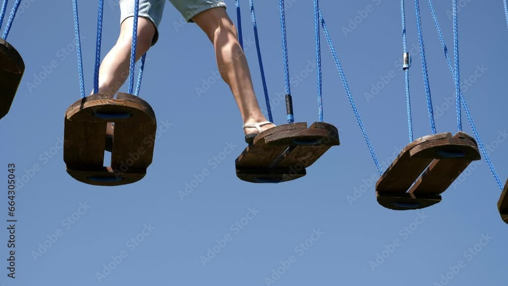 A young, focused woman boldly walks along a swinging suspended walkway ...