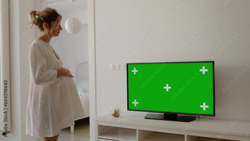 Pregnant woman coming from bedroom watching TV with green screen in ...