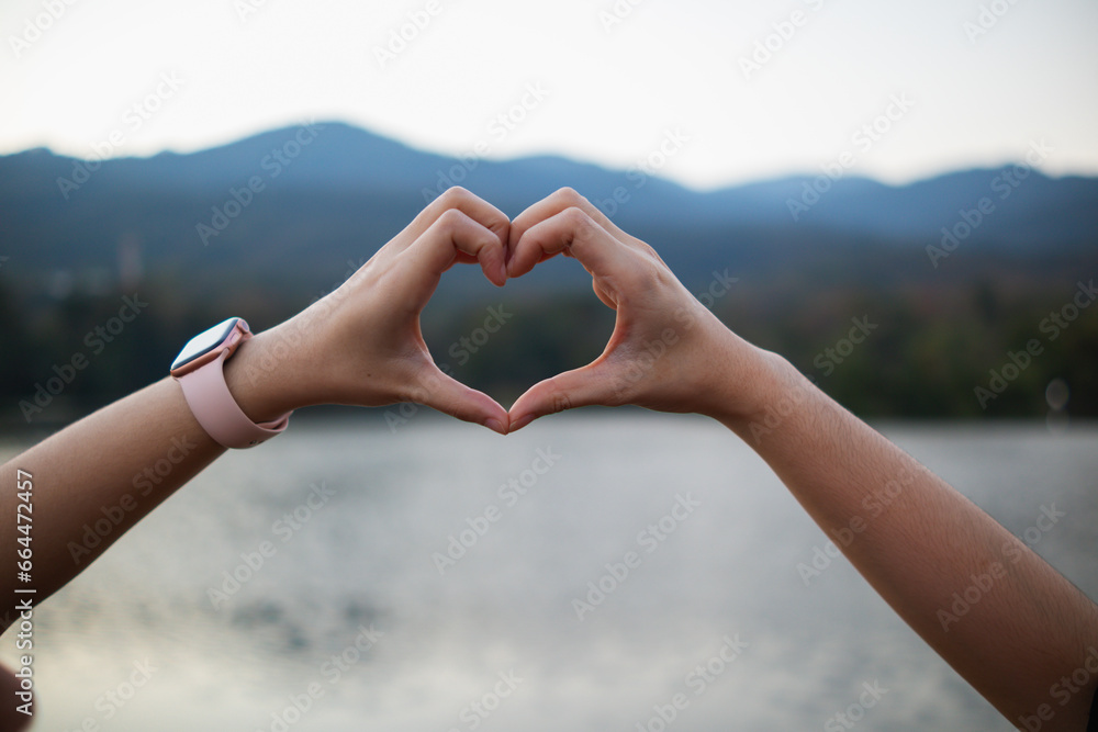 young woman and her friend raised their hands together to form heart ...