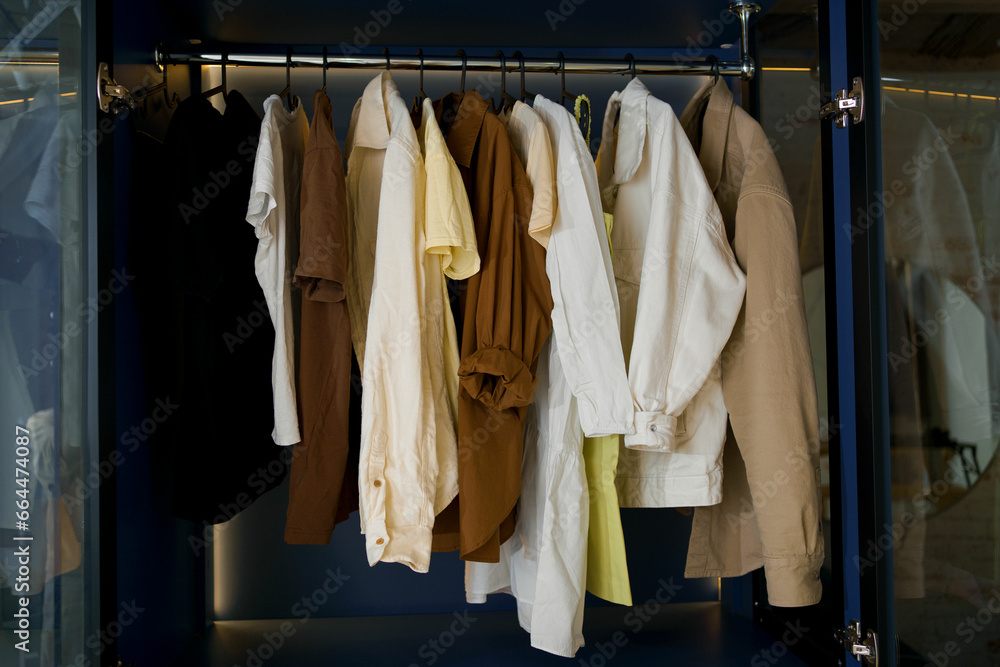 A variety of clothes hang in a cabinet with lighting and glass doors ...