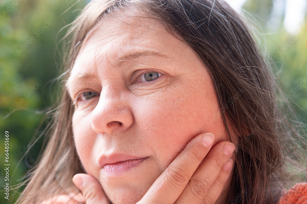 close up of mature female face, woman 50 years old carefully examines ...