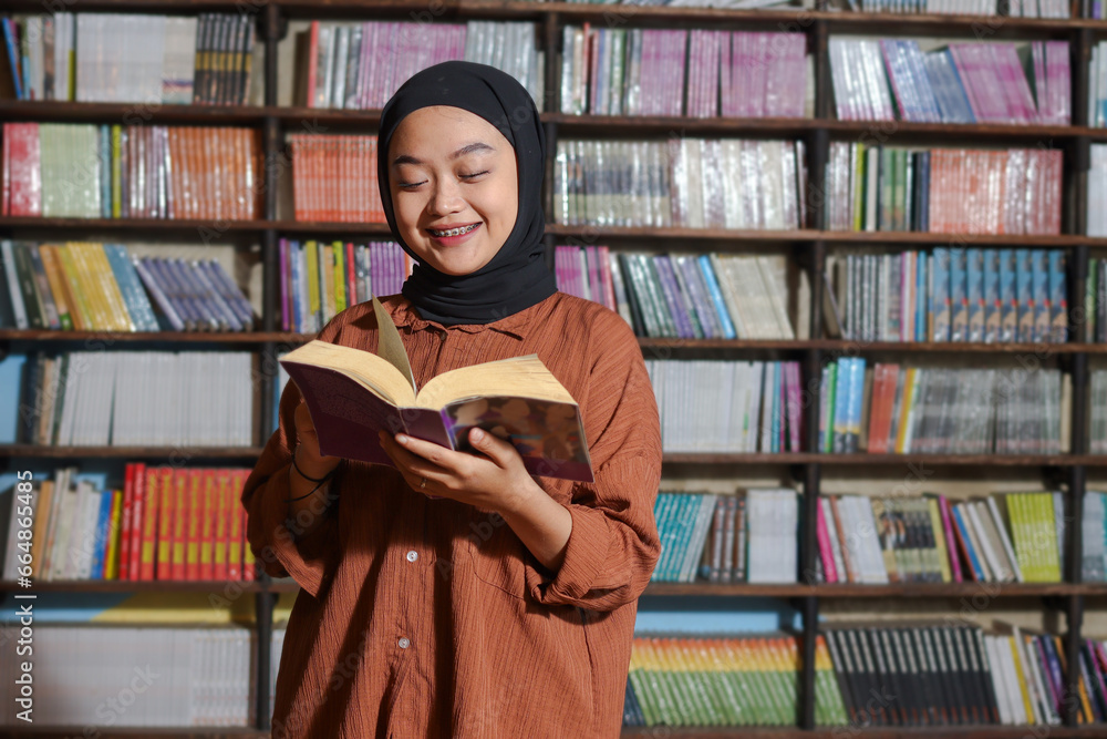 Portrait of Asian hijab woman holding book in front of library ...