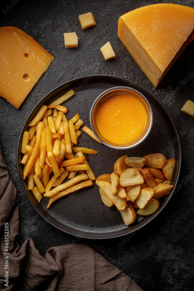 Fried potatoes, fries with cheese sauce on a black plate, dark table ...