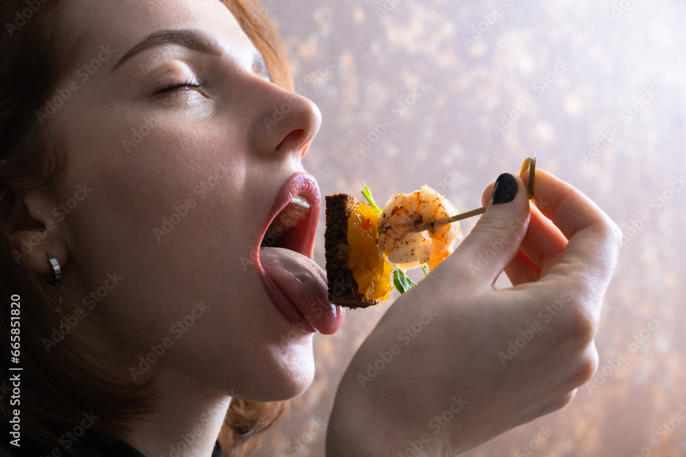 Shrimp and mango chutney canapes in female fingers near open mouth ...