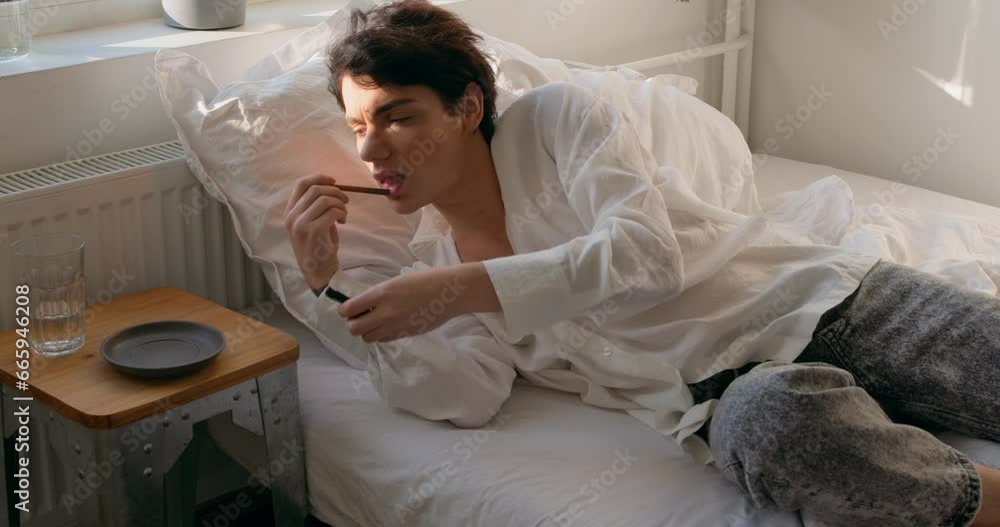 young drunk man smoking weed lying in bedroom. heavy smoker spend time ...