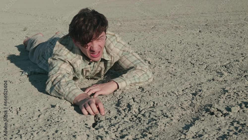 A young man lies on lifeless ground under the rays of the scorching sun ...