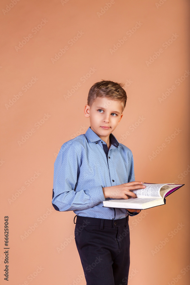 Schoolboy model holding book in hands at beige background, pensive ...