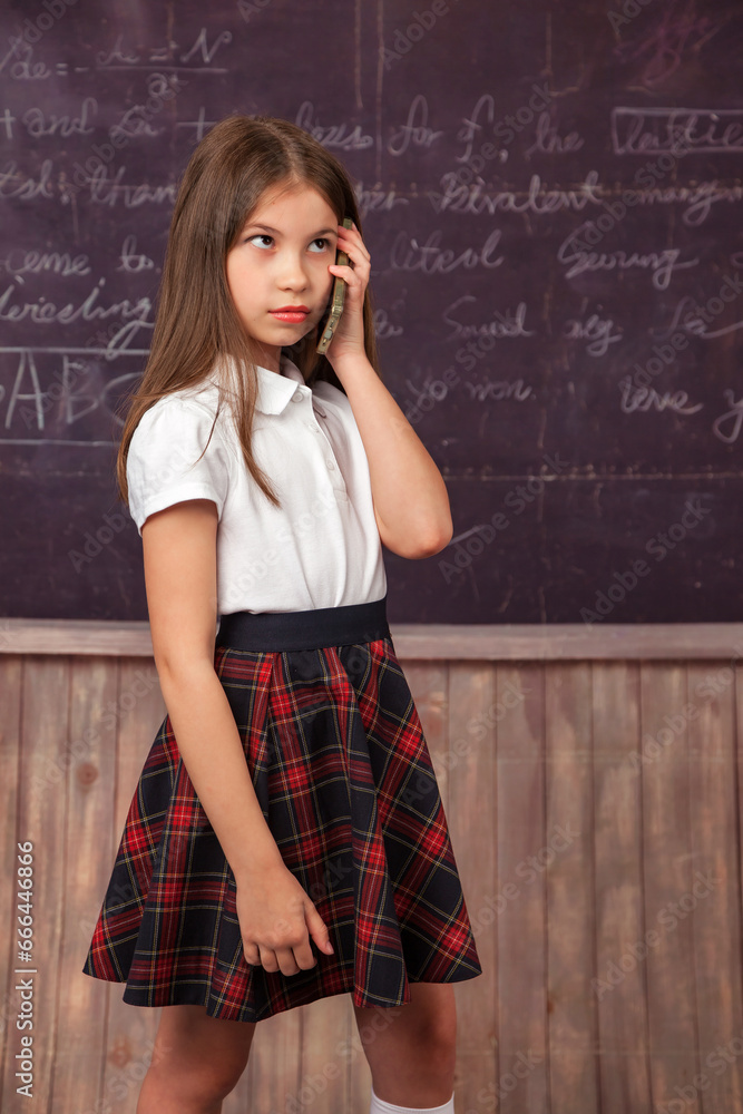 Adorable schoolgirl 7 year old in school uniform calling mobile phone ...