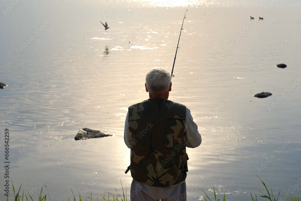 Old man fishing. Senior gray haired fisherman throws a spinning from ...