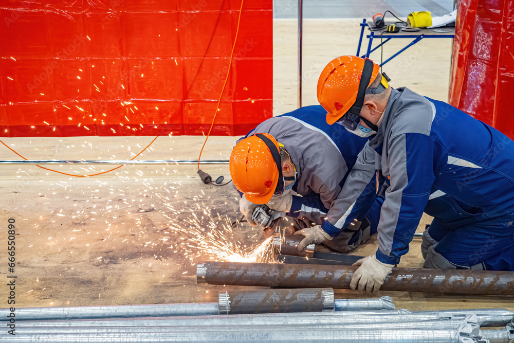 Foto de Men saw steel pipes. Workers collect scaffolding. Guys work ...