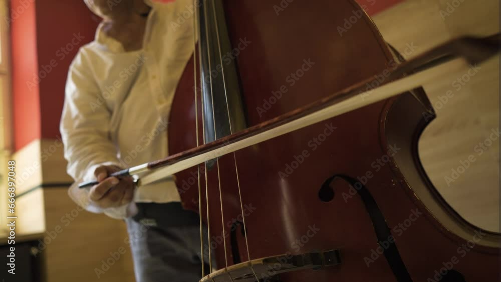 low angle of an olive skin elderly man European playing cello bass with ...
