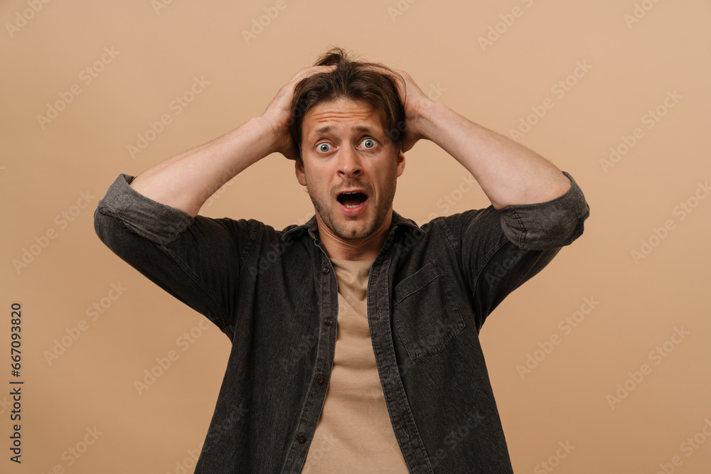 Shocked man grabbing his head isolated over beige wall Stock Photo ...