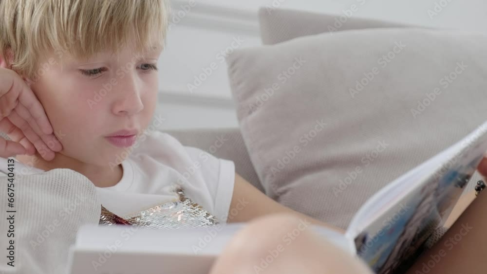 A young boy on a couch reading a book out loud. Small kid reading a ...