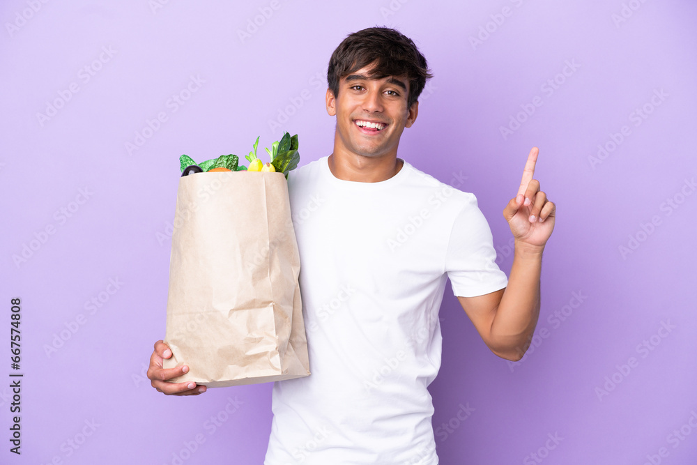 Young man holding a grocery shopping bag isolated on purple background ...