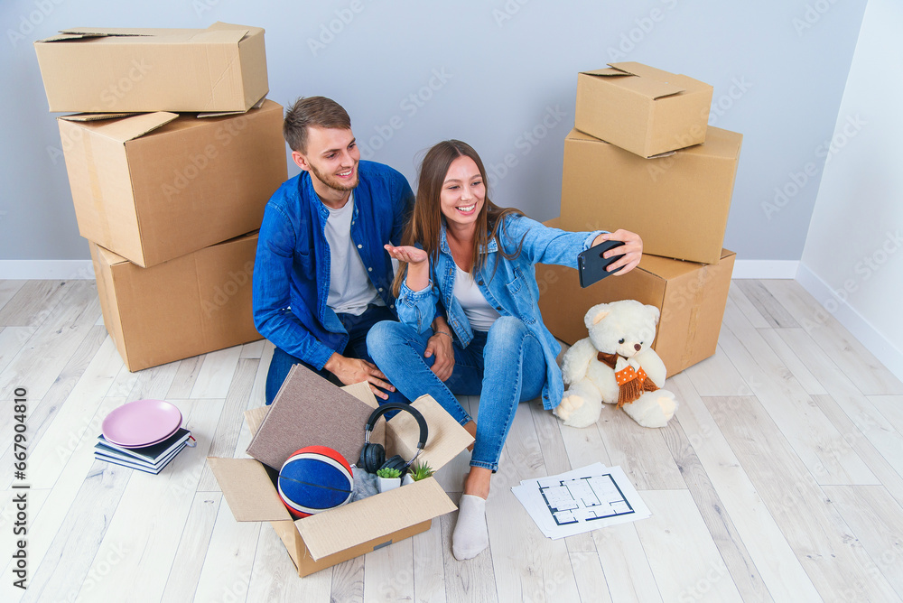 Young couple taking selfies in their new home while sitting among ...