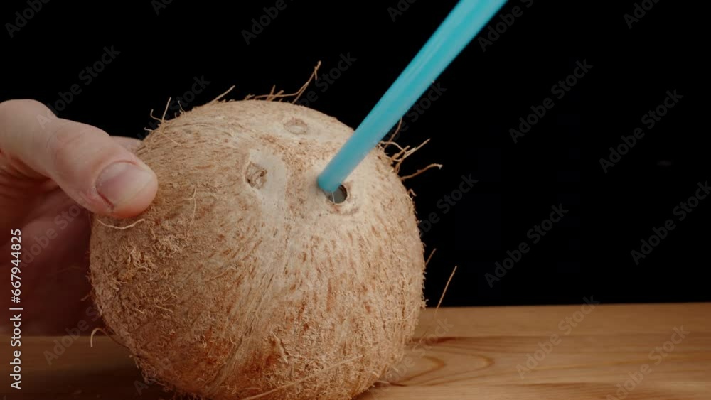 A coconut nut with a drilled hole into which a blue straw is inserted ...