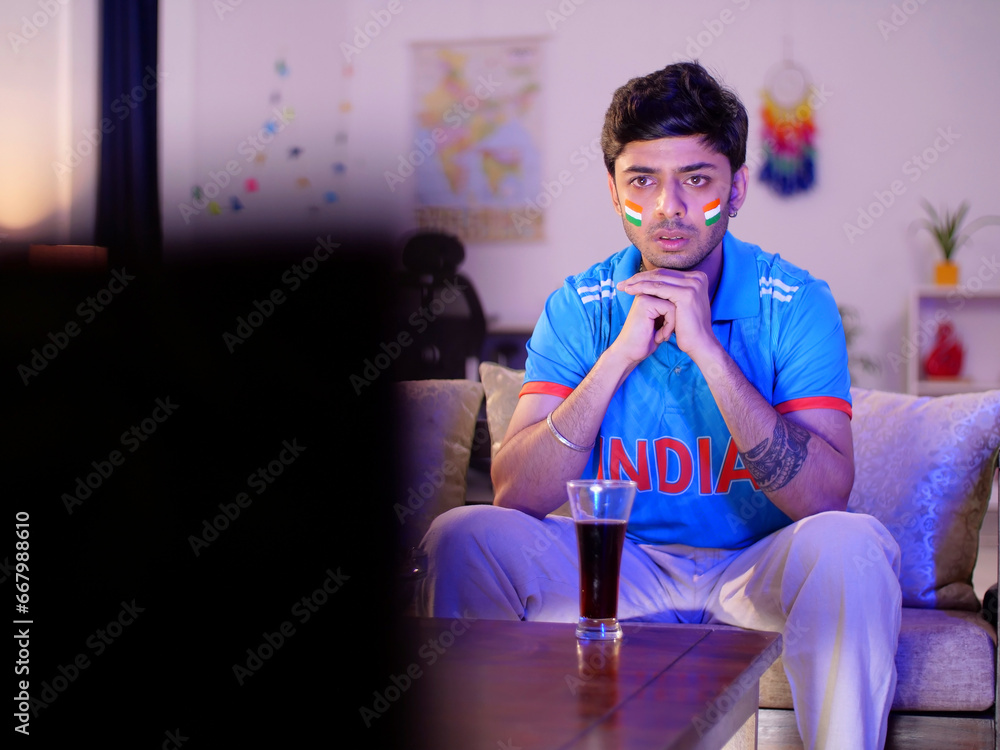An Indian man in a blue cricket jersey watching a live cricket match on ...
