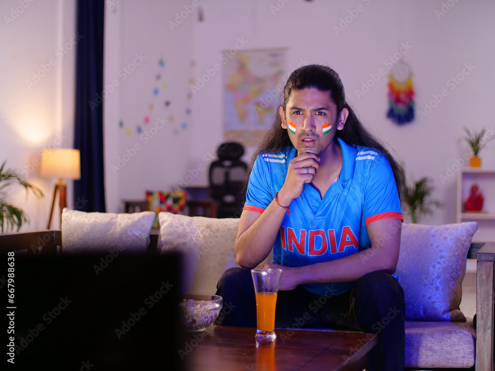 Excited young Indian man with long hair wearing cricket jersey watching ...