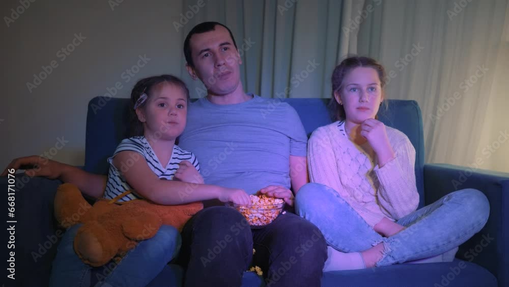 Happy father, his children are watching TV, eating popcorn, smiling ...
