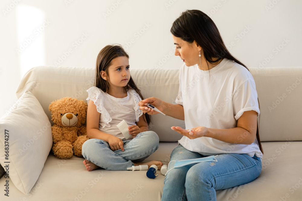 Worried mom treating sick kid suffering from flu and fever, holding thermometer, checking high ...