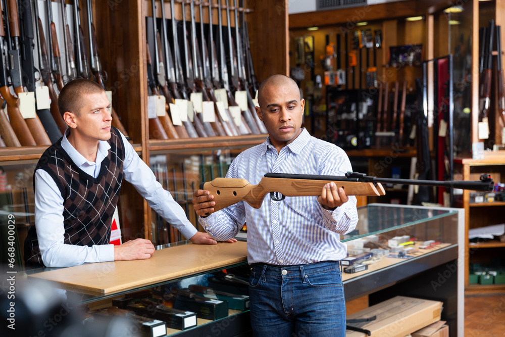 Hispanic man examining hunting break-barrel air rifle in gun shop ...