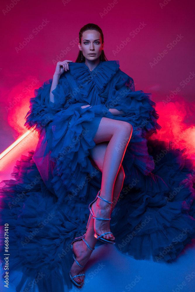 Beautiful model in a lavish blue carnival gown poses in a warmly lit ...