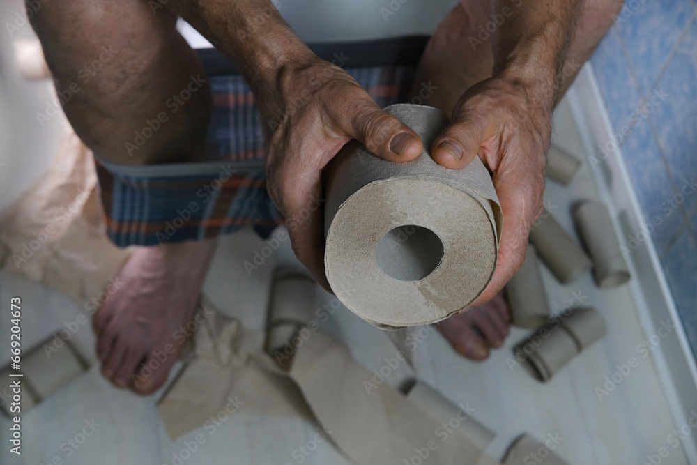 man suffering from diarrhea holds roll of toilet paper while sitting on ...