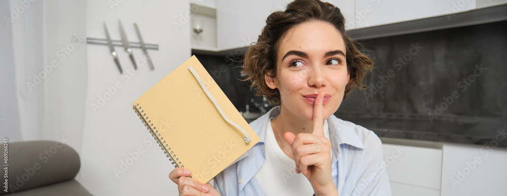 Portrait of cute young woman, holds planner, writes her secrets in ...