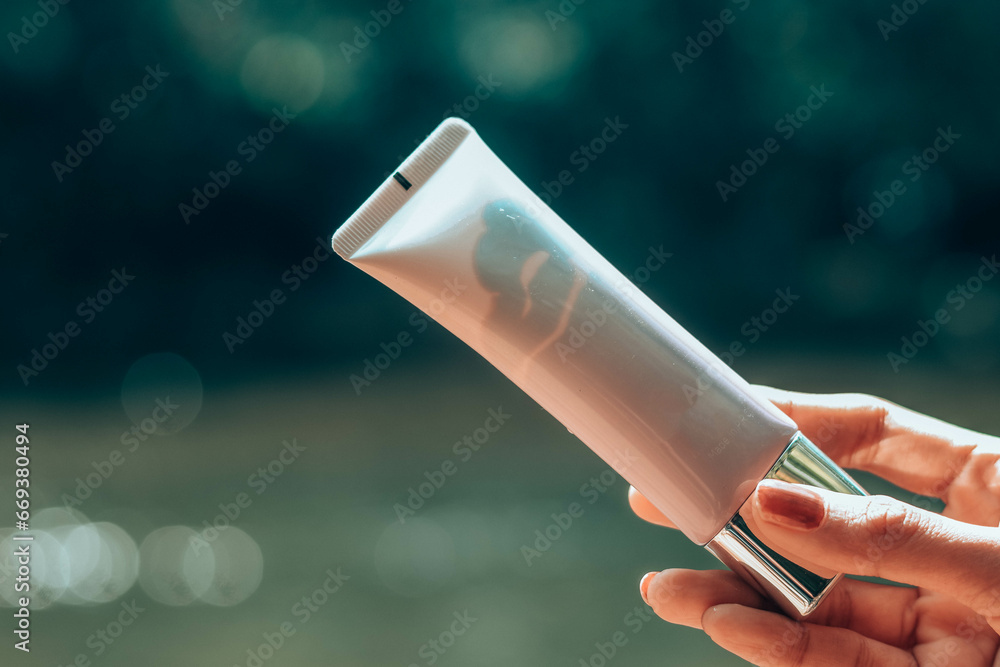 female hand holding a cosmetic product tube in nature river background ...