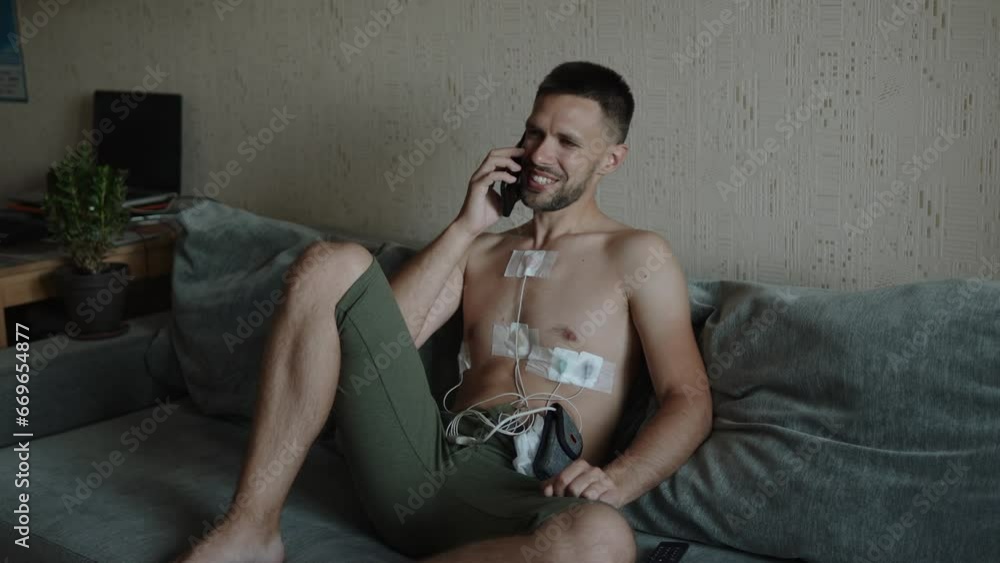 Positive caucasian man with Holter ECG monitoring device sits on sofa ... Positive caucasian man with Holter ECG monitoring device sits on sofa ...