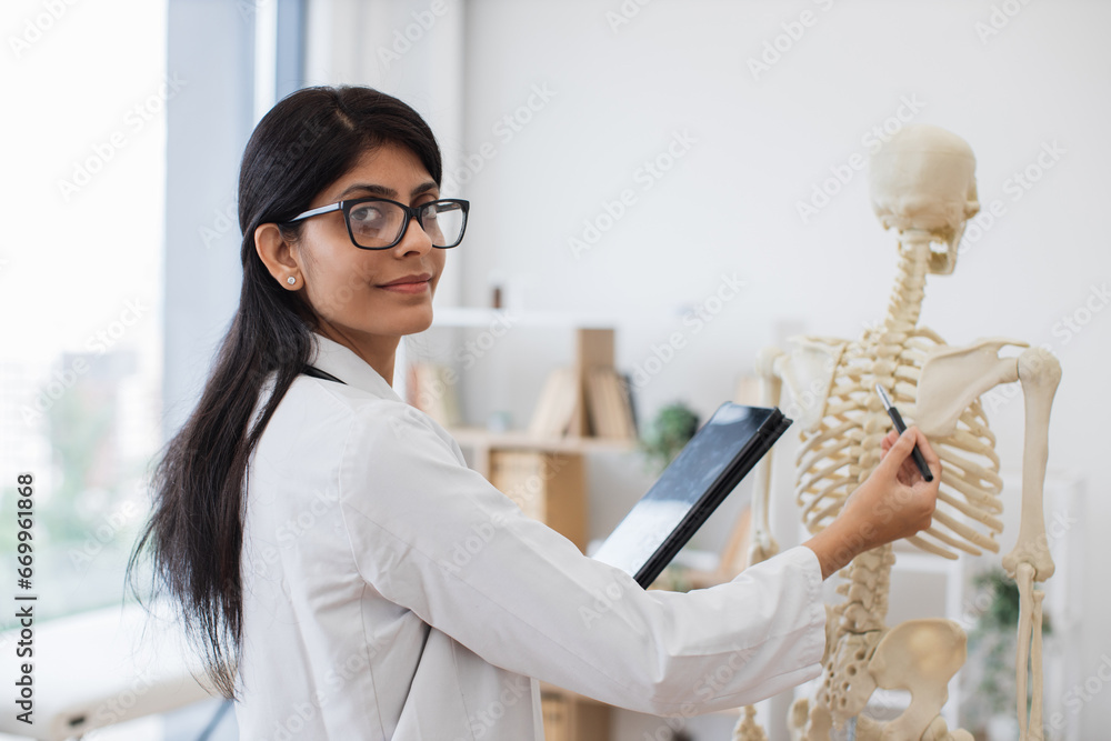 Side view of hindu medical worker with tablet pointing at spine while ...