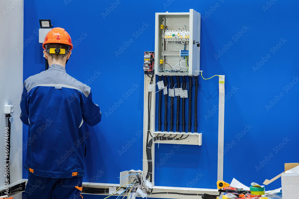 Man electrician at work. Guy fixes electrical equipment. Wall with ...