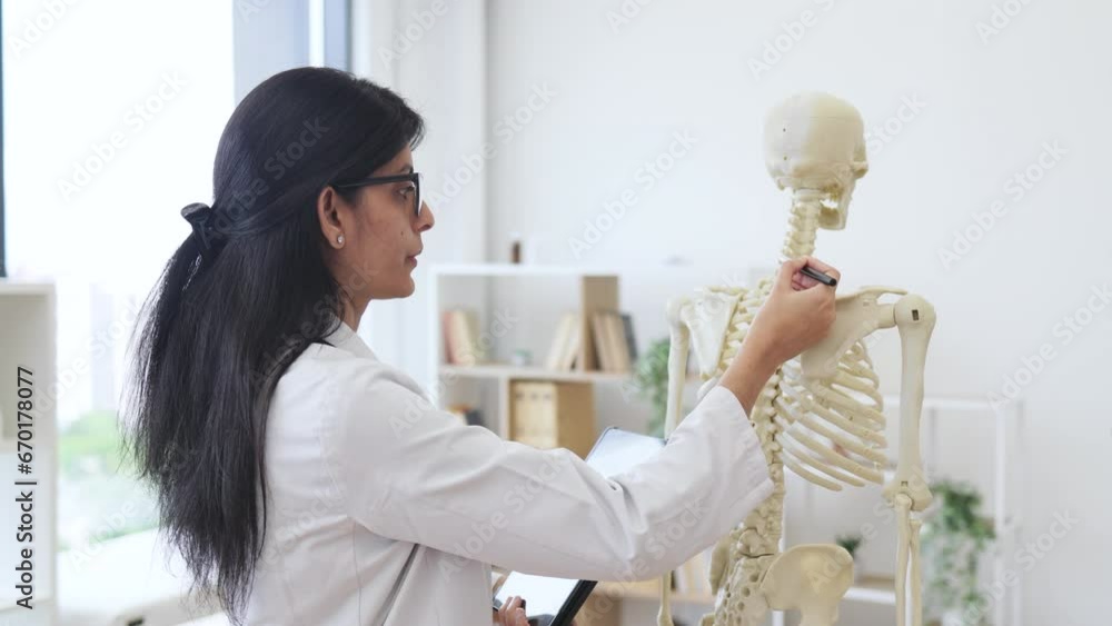 Side view of hindu medical worker with tablet pointing at spine while ...