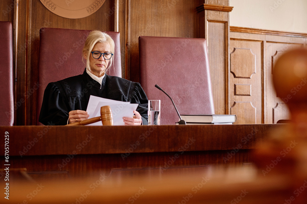 Experienced female judge in black gown reading juridical paper ...