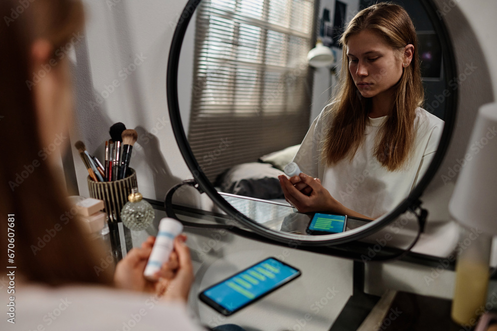 Reflection in mirror of stressed teenage girl looking at bottle of ...