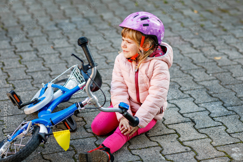 Cute little girl sitting on the ground after falling off her bike ...