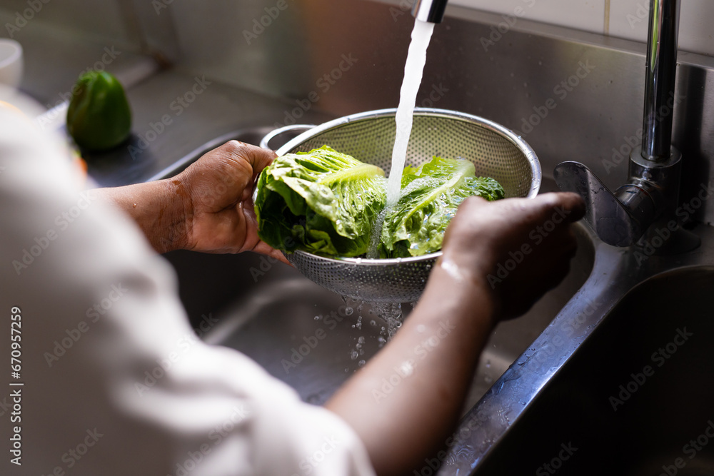 African american male chef washing vegetables in sink in restaurant ...