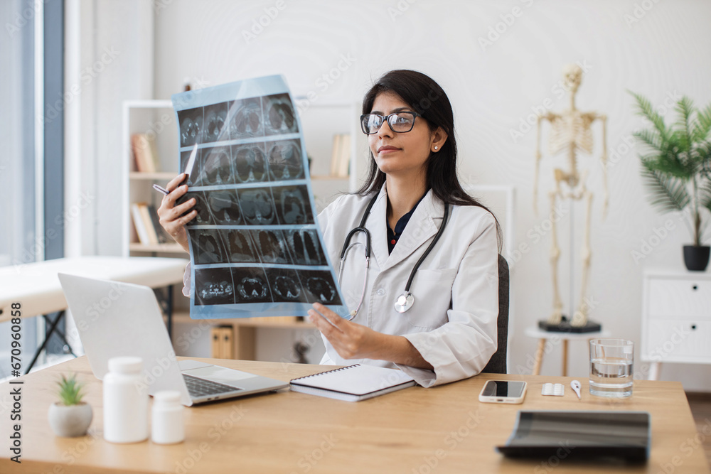 Serious hindu woman wearing white coat and stethoscope studying CT ...